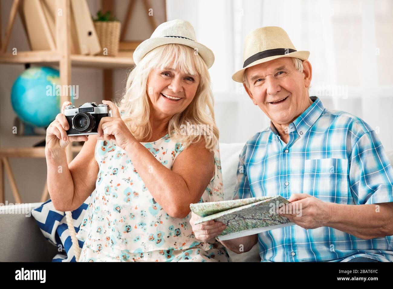 Senior couple sitting in travel agency sitting wearing hats holding ...