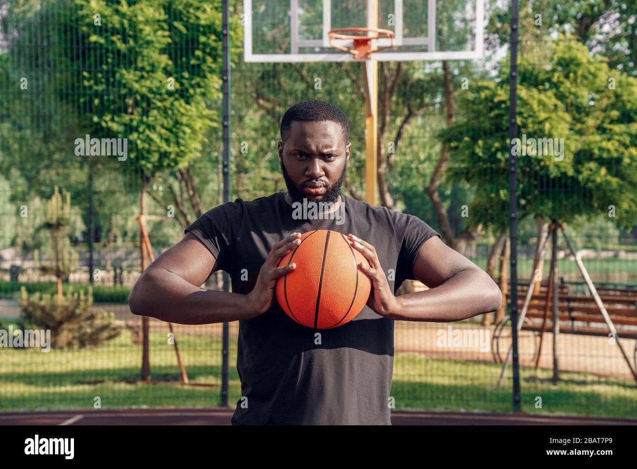 Outdoors Activity. African man standing squeezing ball on basketball ...