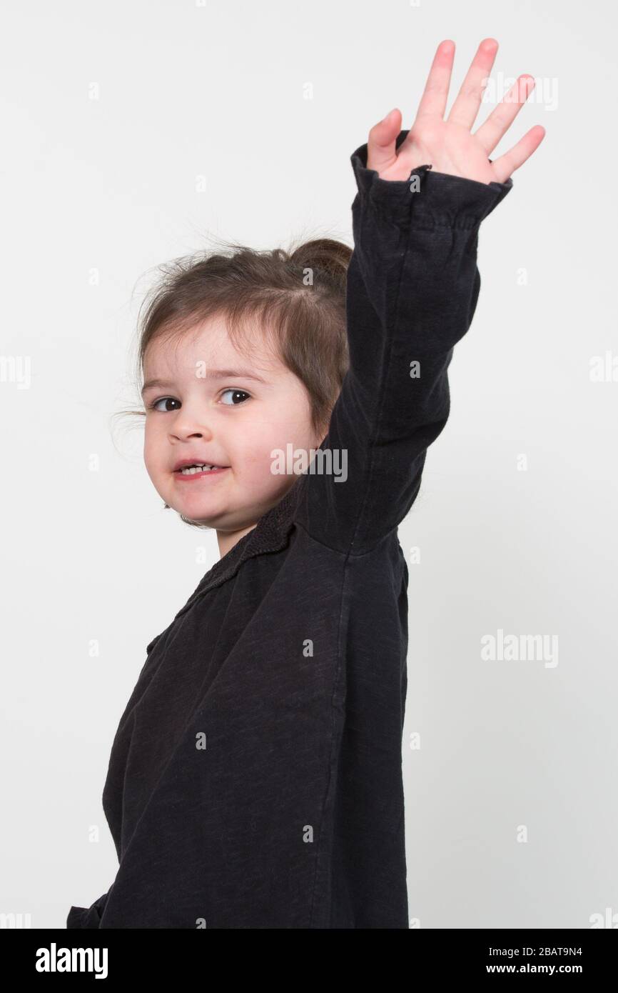 a young pretty child girl raises her arm and hand to grab something ...