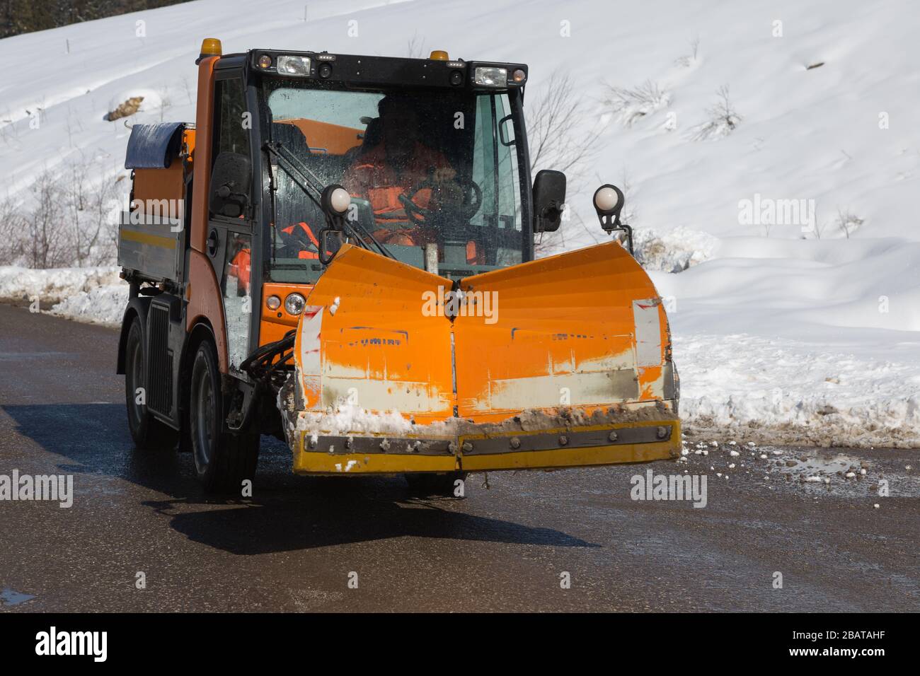Orange-coloured Snowplough Operating on the Road with Snow on the Edges ...
