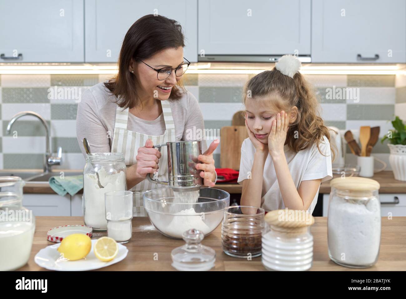 Mother and child preparing bakery together in home kitchen. Woman sifts ...