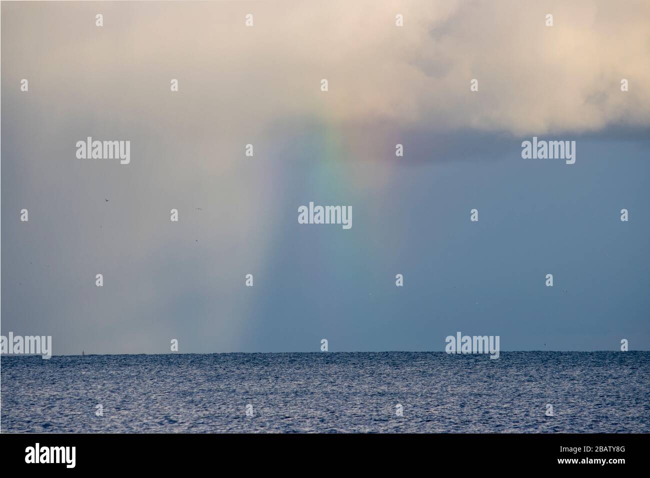 A rainbow appears as sun shines through rain clouds across the sea ...