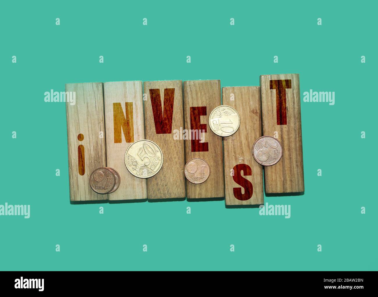 Invest text written on wooden block with coins on teal background ...