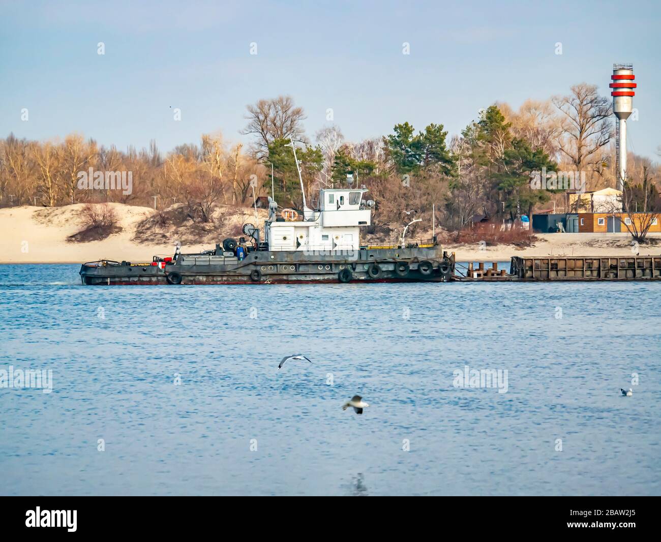 A tugboat pushes a barge along the water surface of the river Stock ...