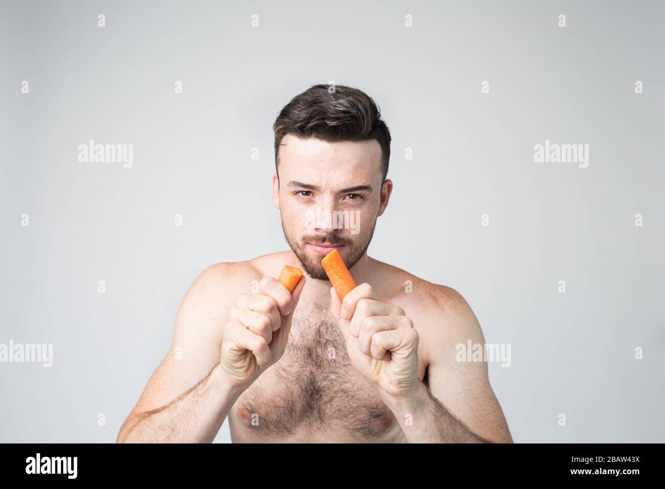 Young man isaolted over background. Confident guy eating carrot ...