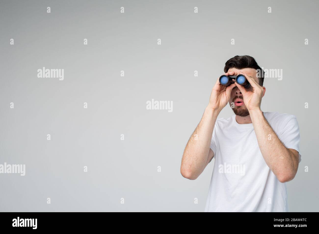 Young man isolated over background. Guy look a binoculars far away ...