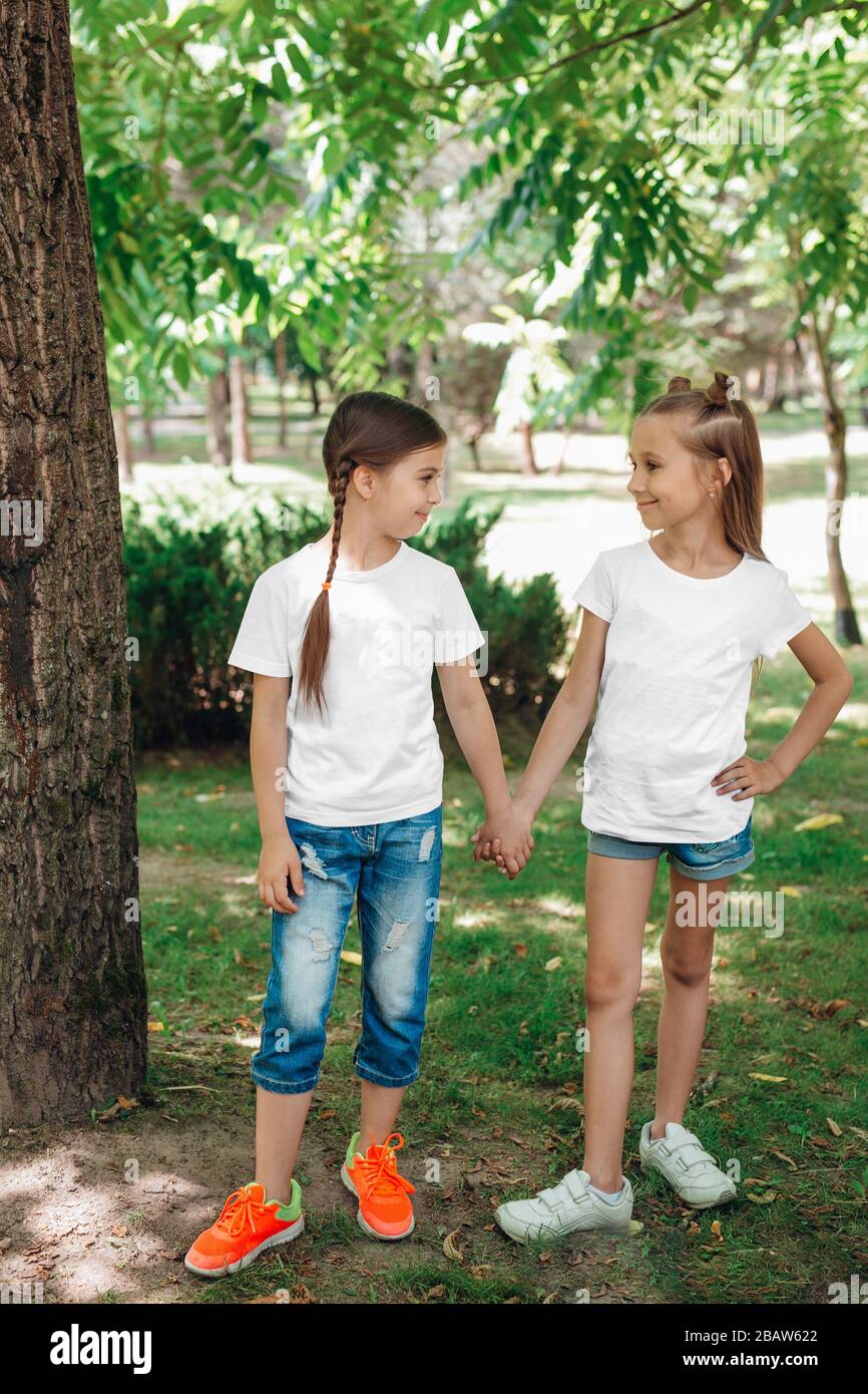 Two little girls in white t-shirts stand holding hands in park outdoor ...