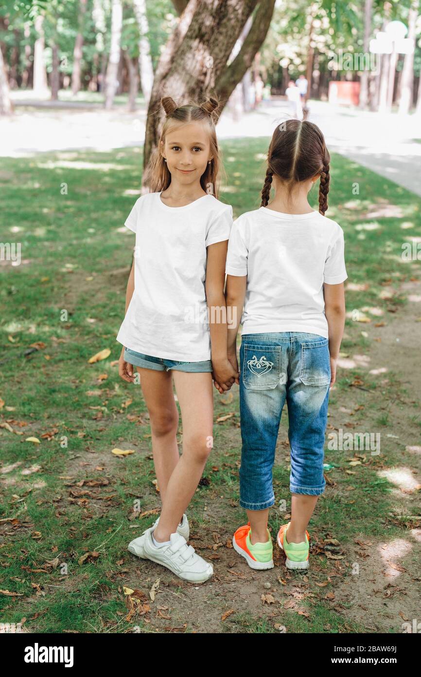 Two little girls in white t-shirts standing in park outdoor. Mock up ...