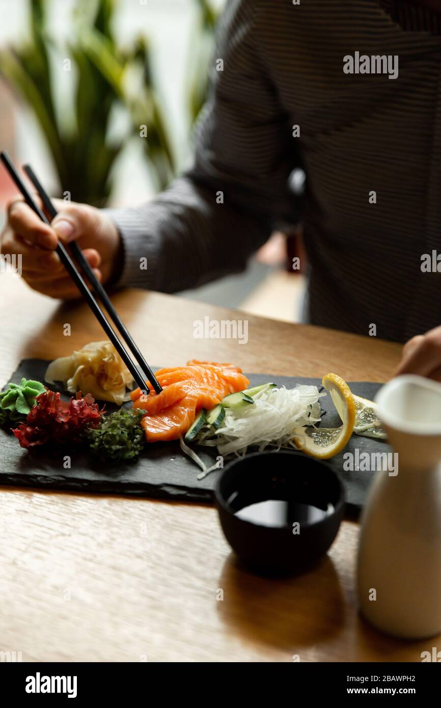 Man holding a chopstick with salmon sashimi on restaurant table. Asian ...