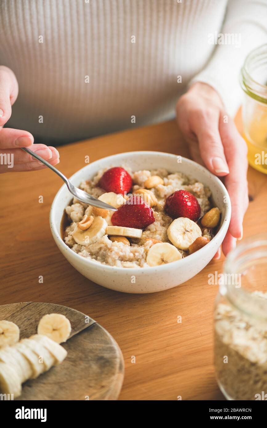 Female eating oatmeal porridge with banana and strawberry for breakfast ...