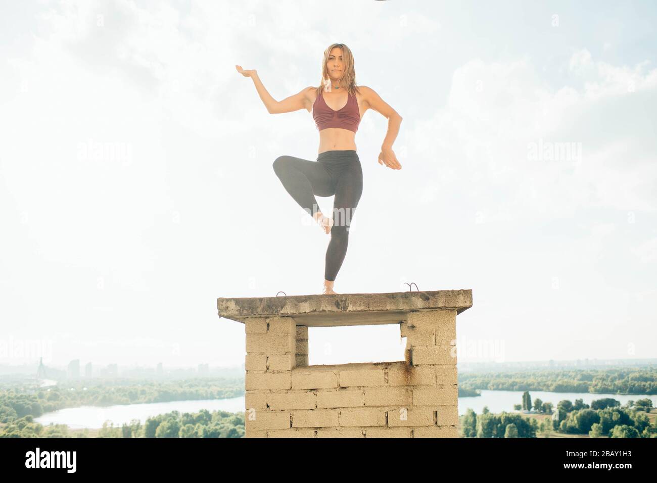 Young woman practices yoga outside. Calm girl on roof. She stand on one ...