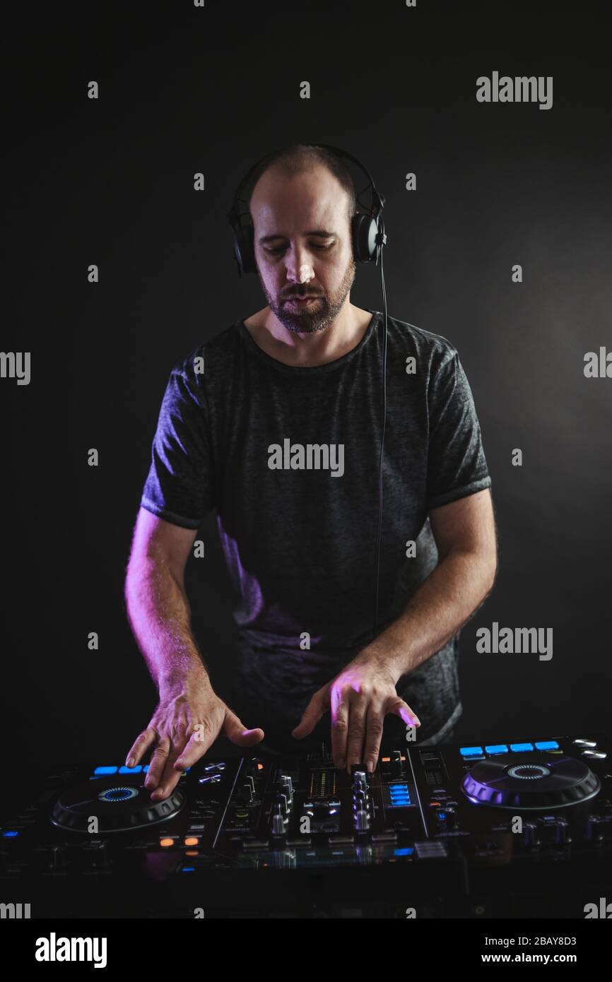 Vertical picture of a male DJ working under the lights against a dark ...