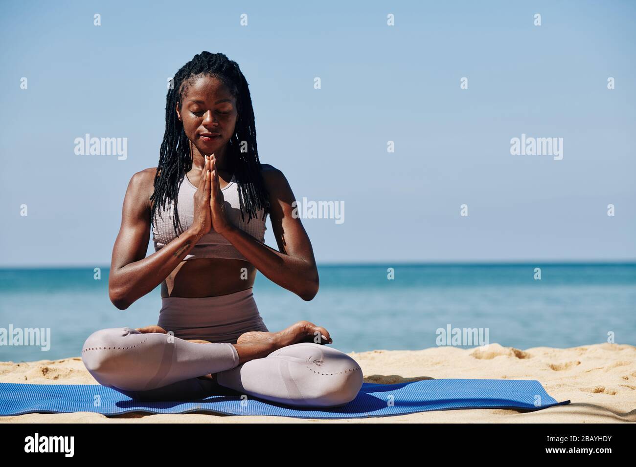 Beautiful slim young woman meditating in lotus position on the beach ...