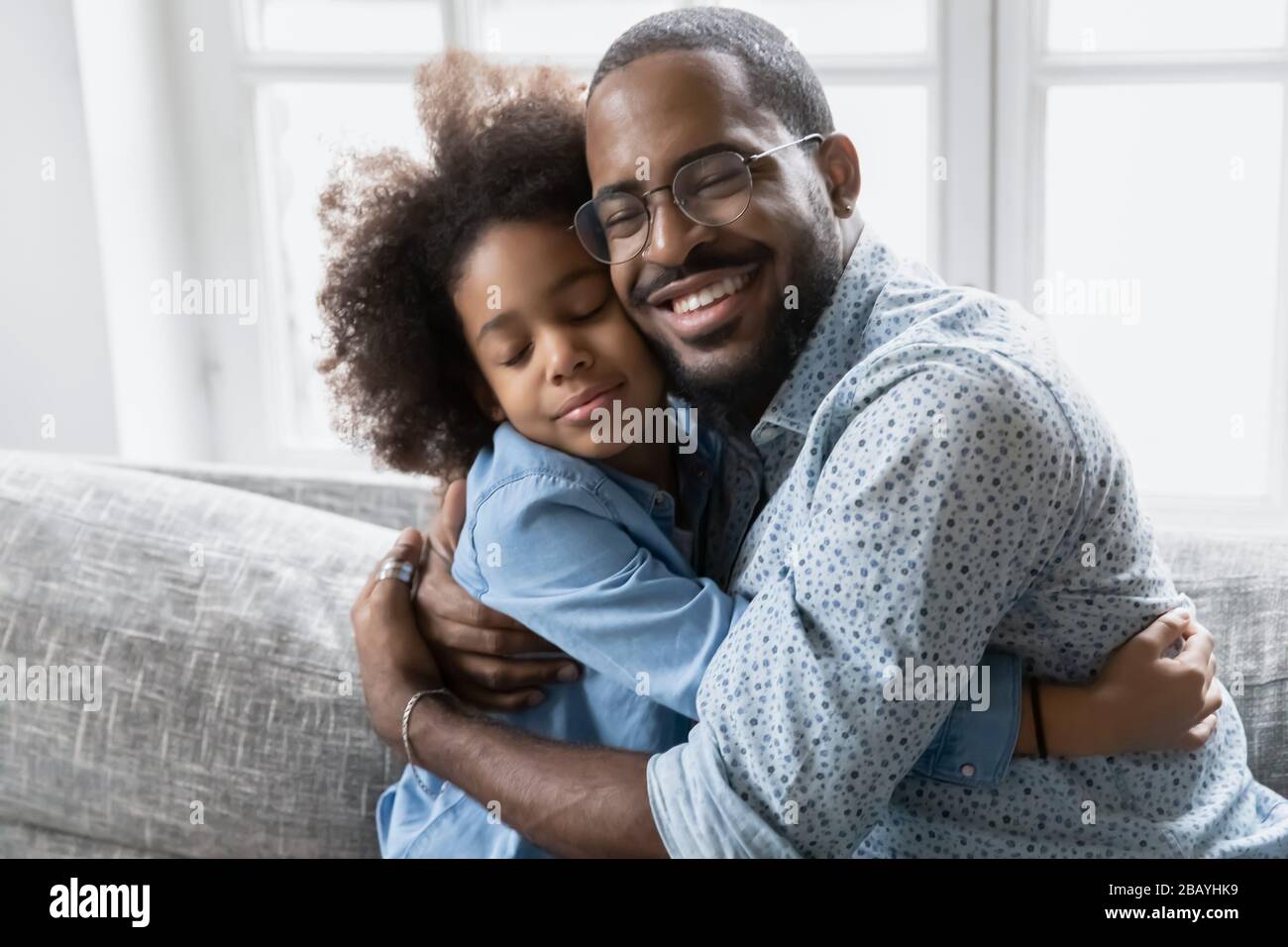 Loving African father sitting on couch hugs little daughter Stock Photo ...