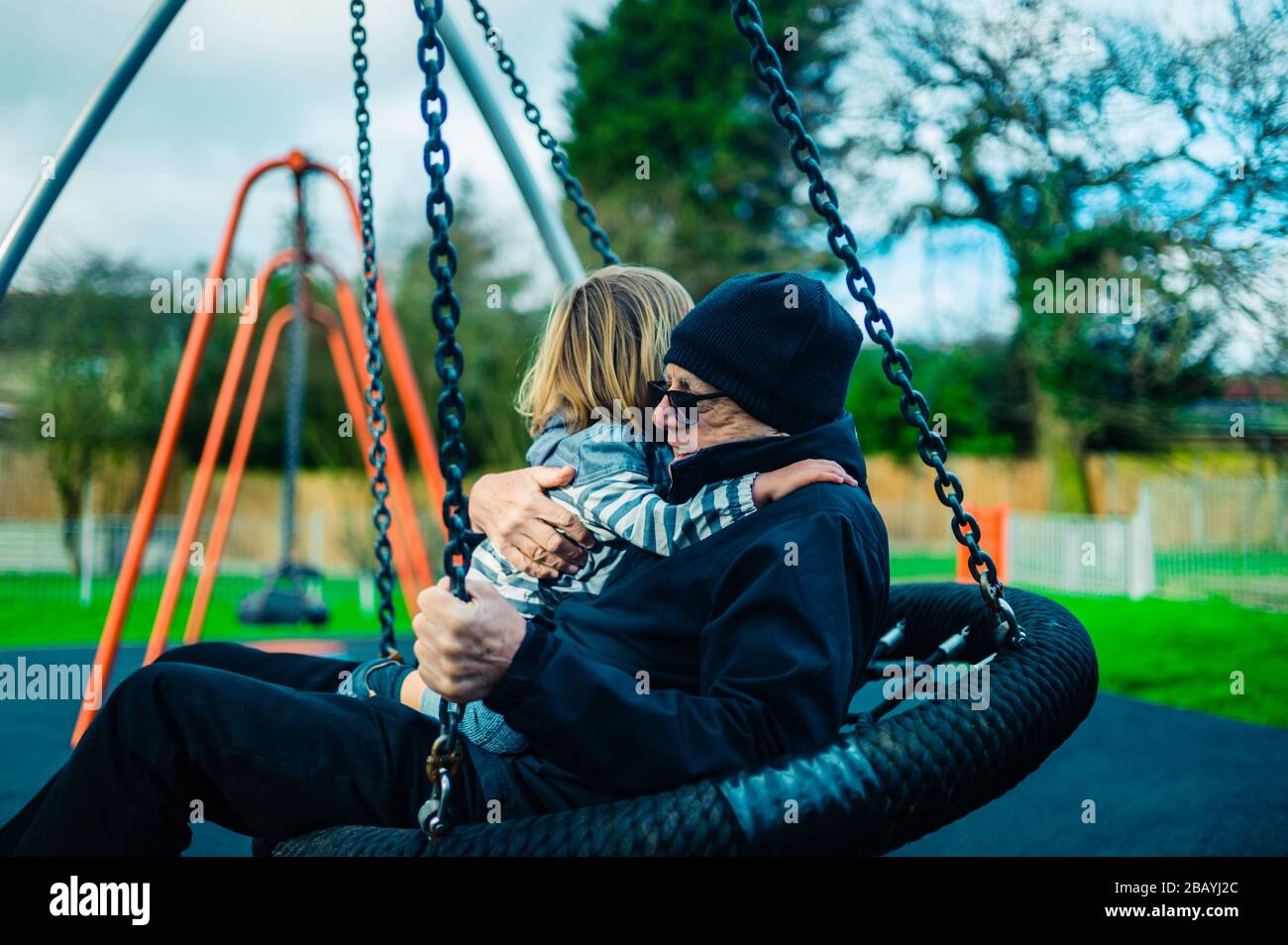 A little preschooler is playing with his grandfather on a spider swing ...