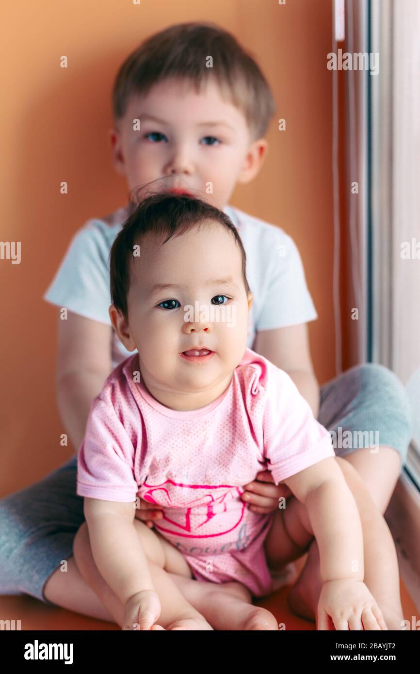 elder brother hugging his baby sister playing and smiling together ...