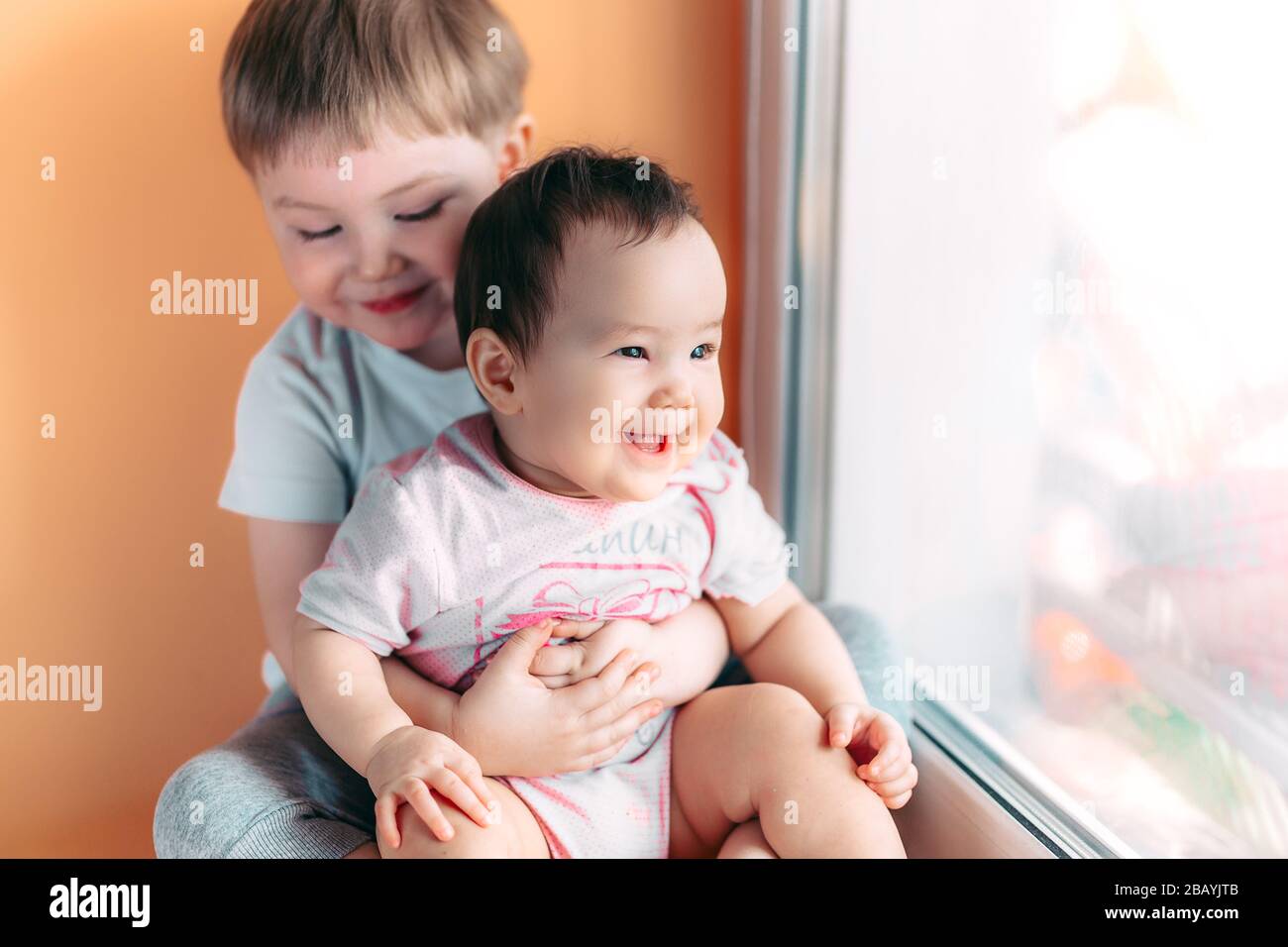 elder brother hugging his baby sister playing and smiling together ...