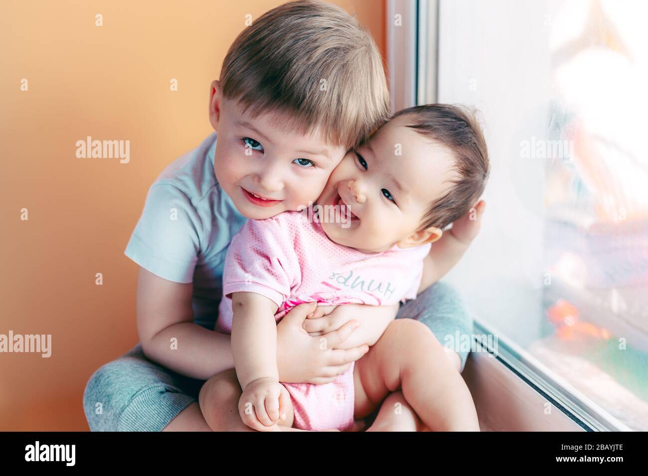 elder brother hugging his baby sister playing and smiling together ...