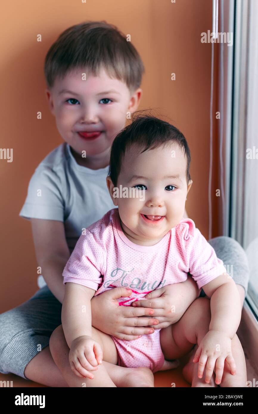 elder brother hugging his baby sister playing and smiling together ...