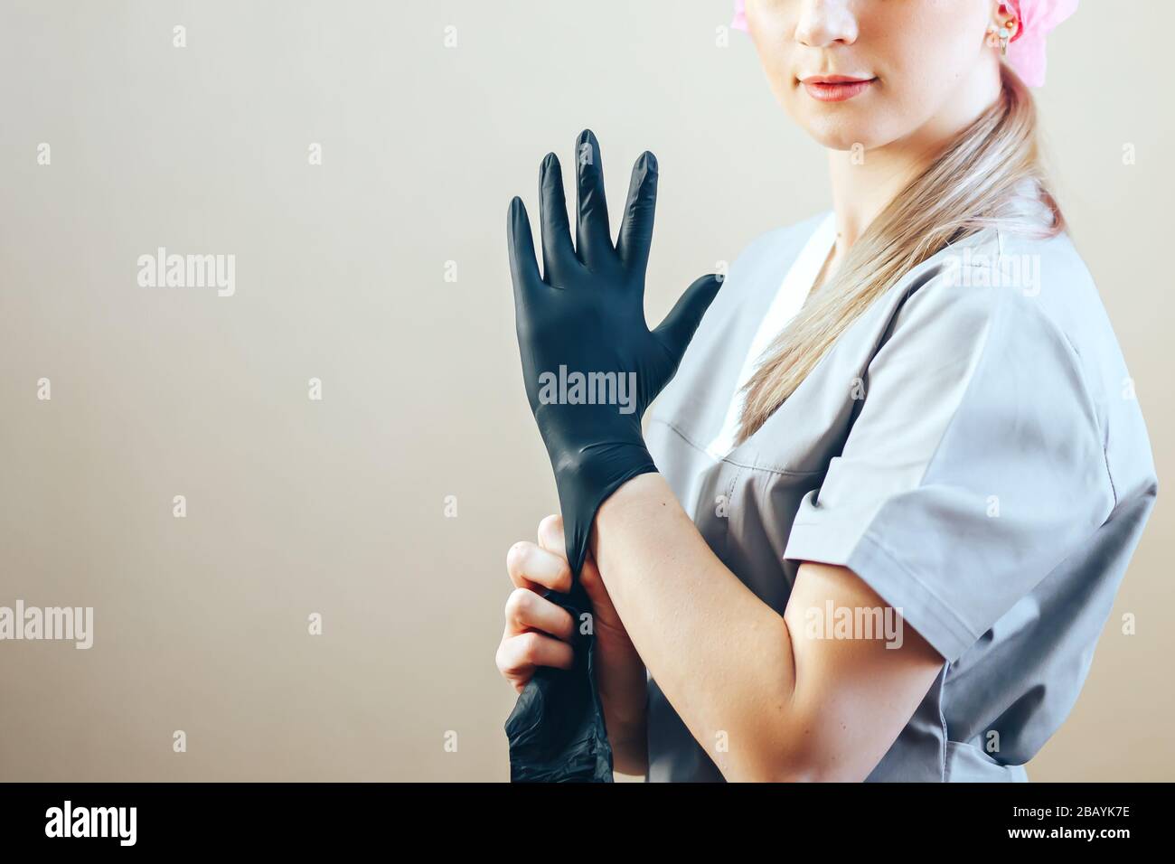 Beautician woman putting on black rubber gloves, she in grey blue ...