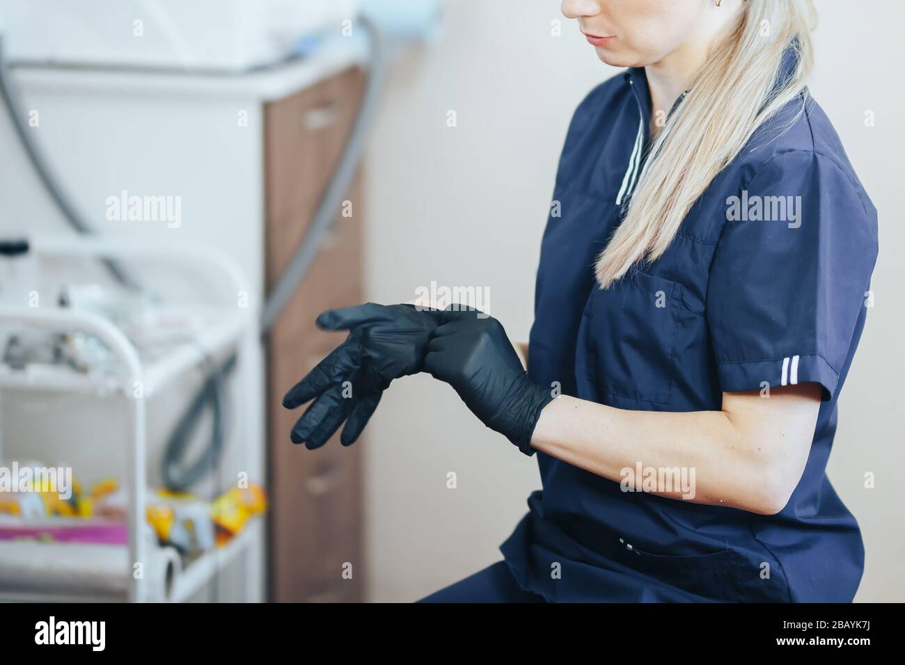 Beautician woman putting on black rubber gloves, she in grey blue ...