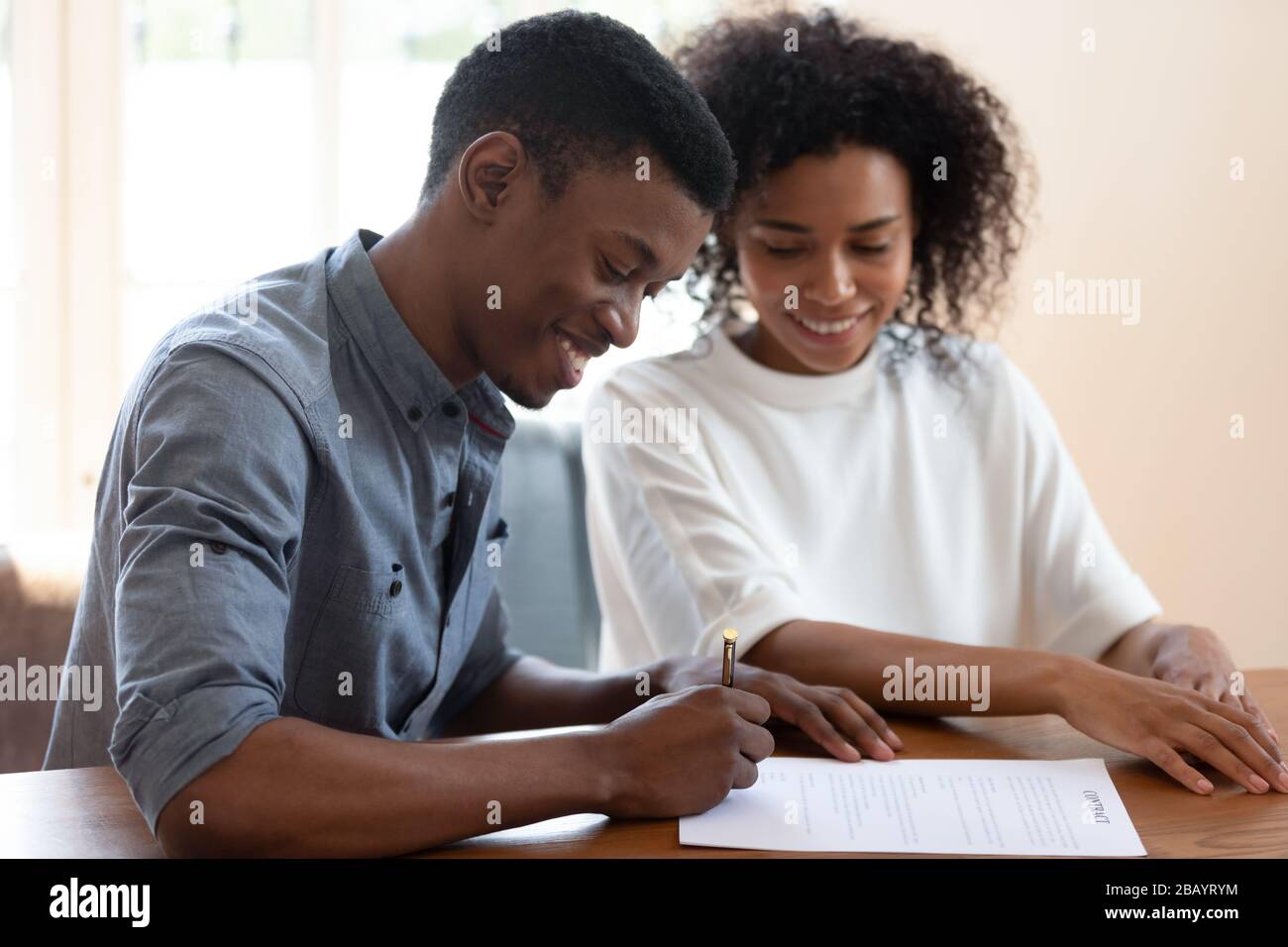 Satisfied African ethnicity couple putting signature on lease agreement ...