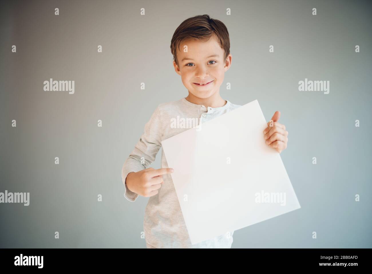 cool young boy holding white sign in front of grey background during ...