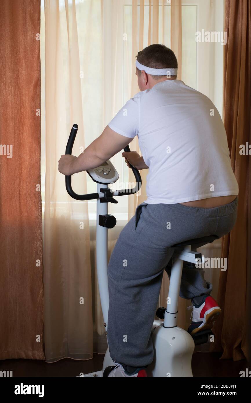Fat guy exercising on stationary training bicycle at home Stock Photo ...