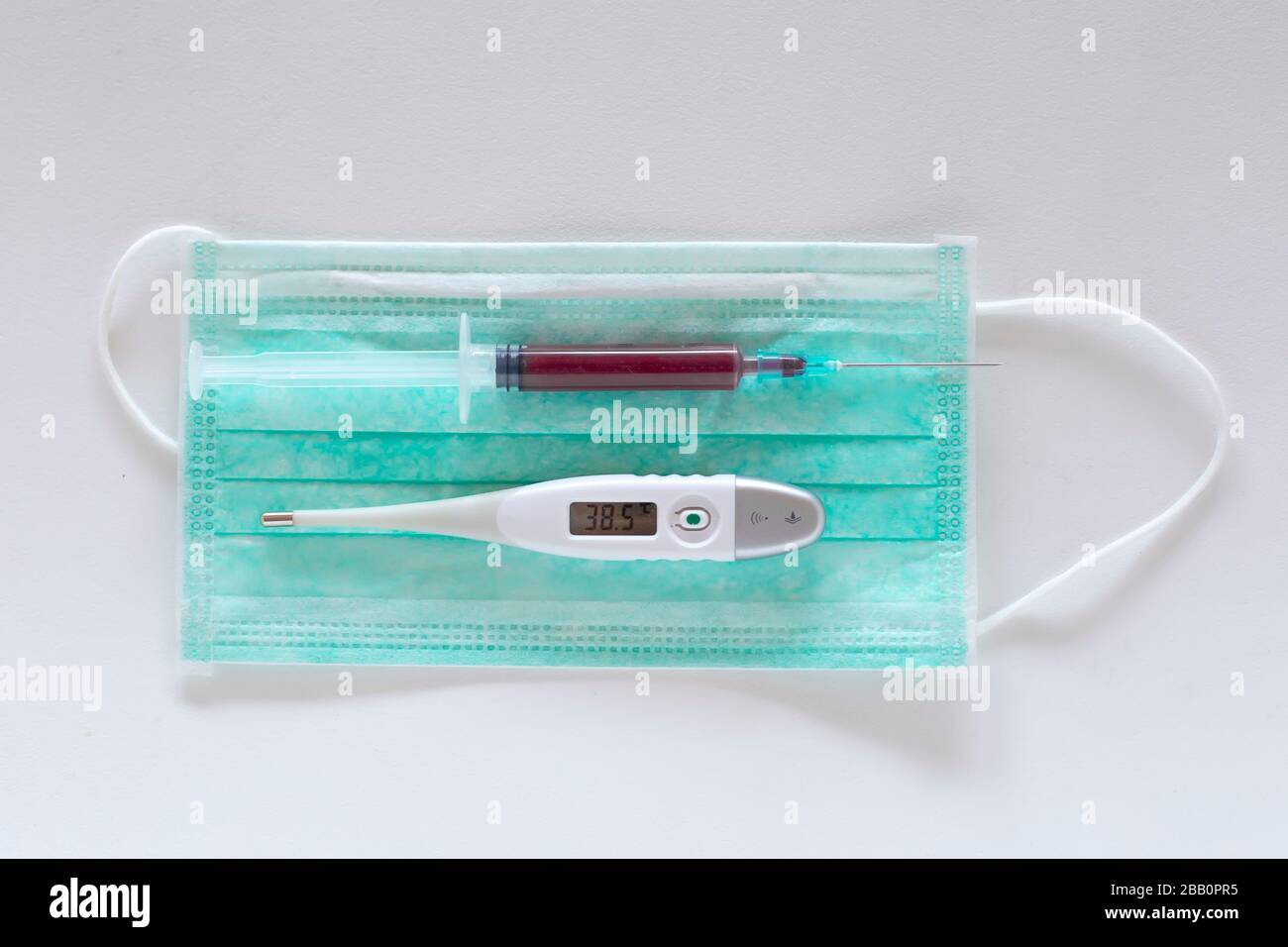 Surgical ear-loop mask, injection syringe and thermometer on the table ...
