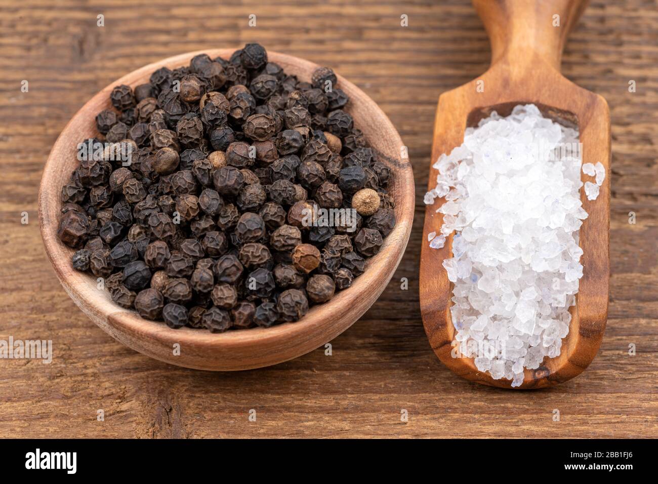 Coarse crystal salt on a small olive wood spice shovel and whole black ...