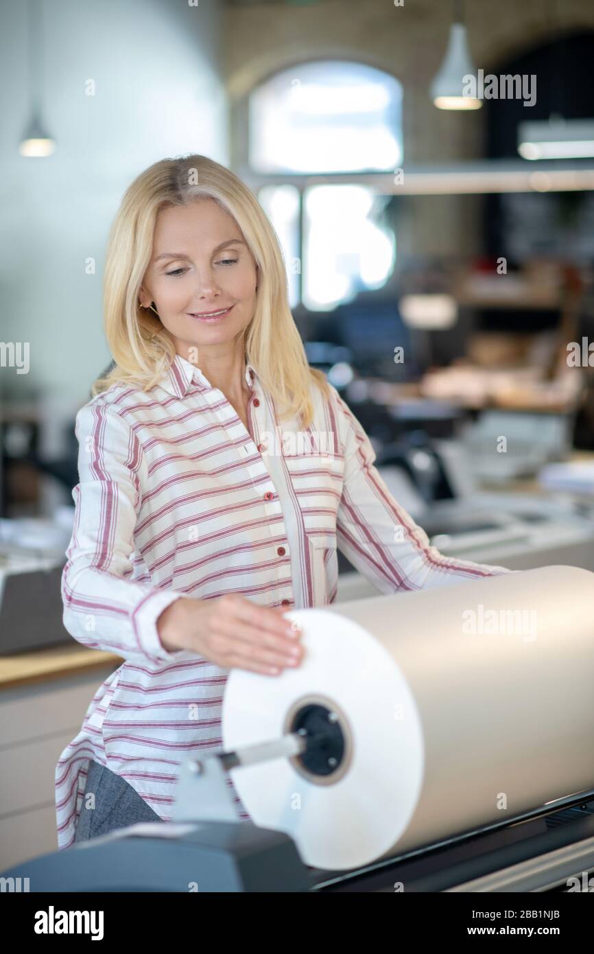 Blonde woman standing at paper roll machine, holding paper roll Stock ...
