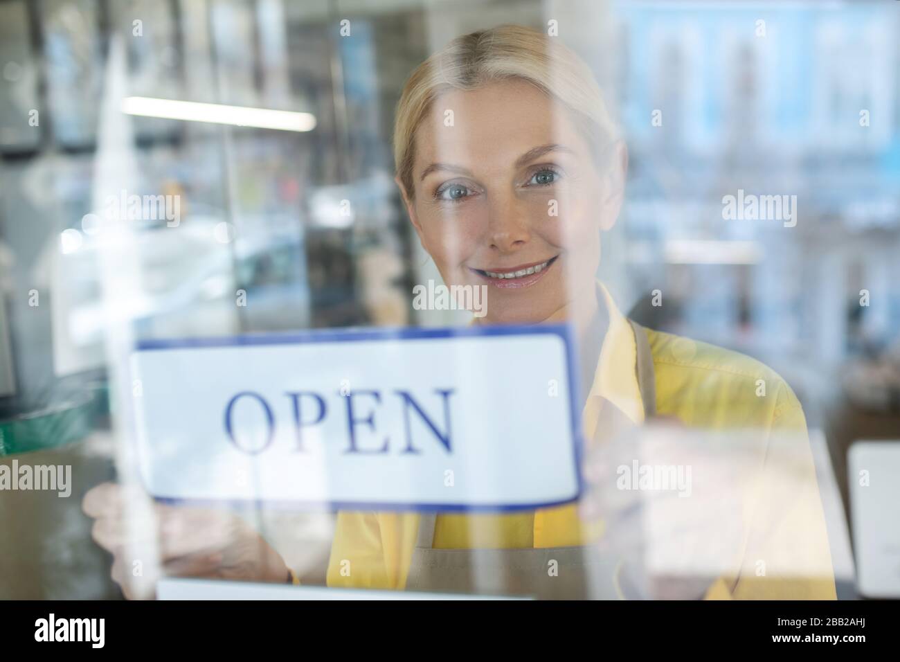 Blonde woman standing behind glass door, holding sign saying open Stock ...