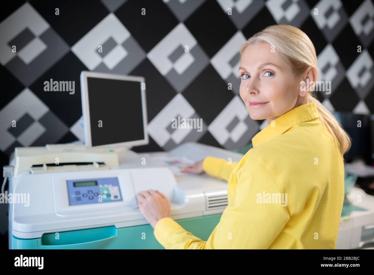 Blonde woman adjusting printing machine, looking into the camera Stock ...