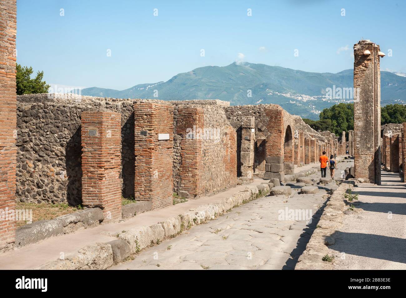 Tourists walk along the cobbled streets between the ruined buildings of ...