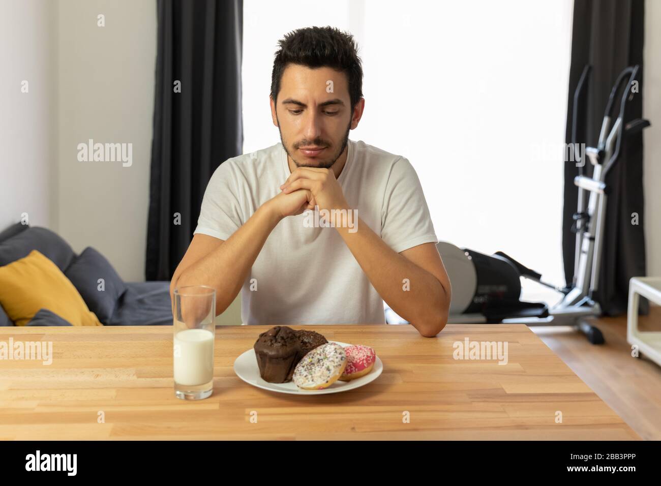 Young handsome guy sits at a table and eats donuts with milk for ...