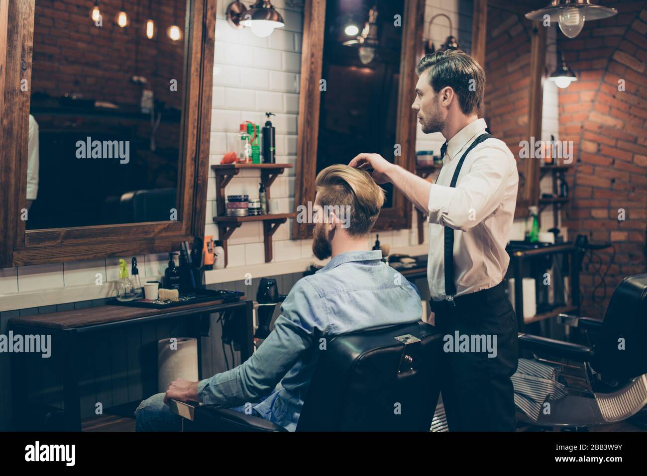 Barber shop classy dressed stylist is working for a perfect hairdo of a ...