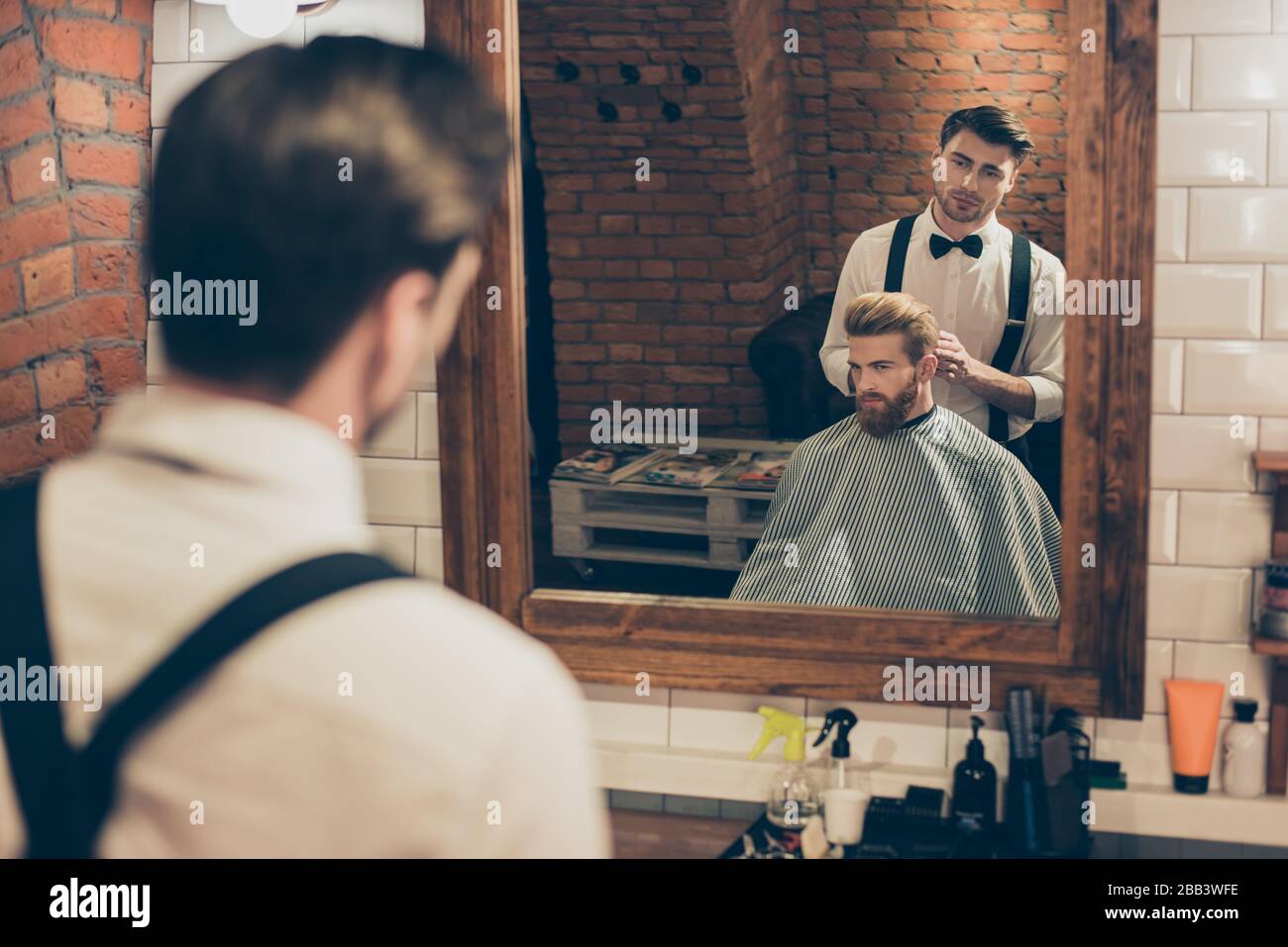 Handsome classy dressed barber shop stylist is presenting the result of ...