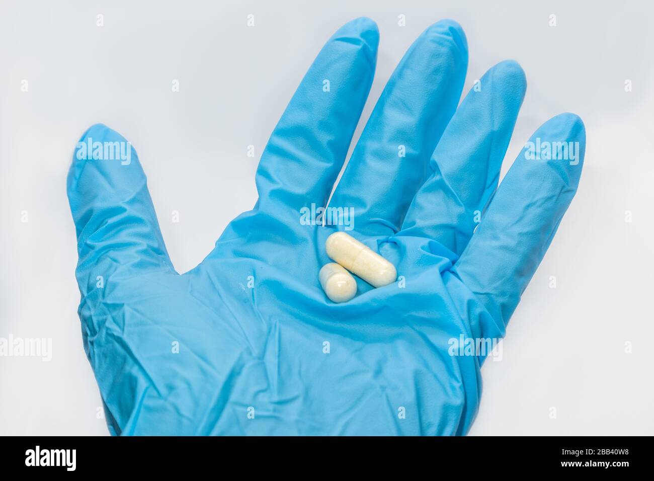 Hand in blue glove takes white supplements long capsules on white ...