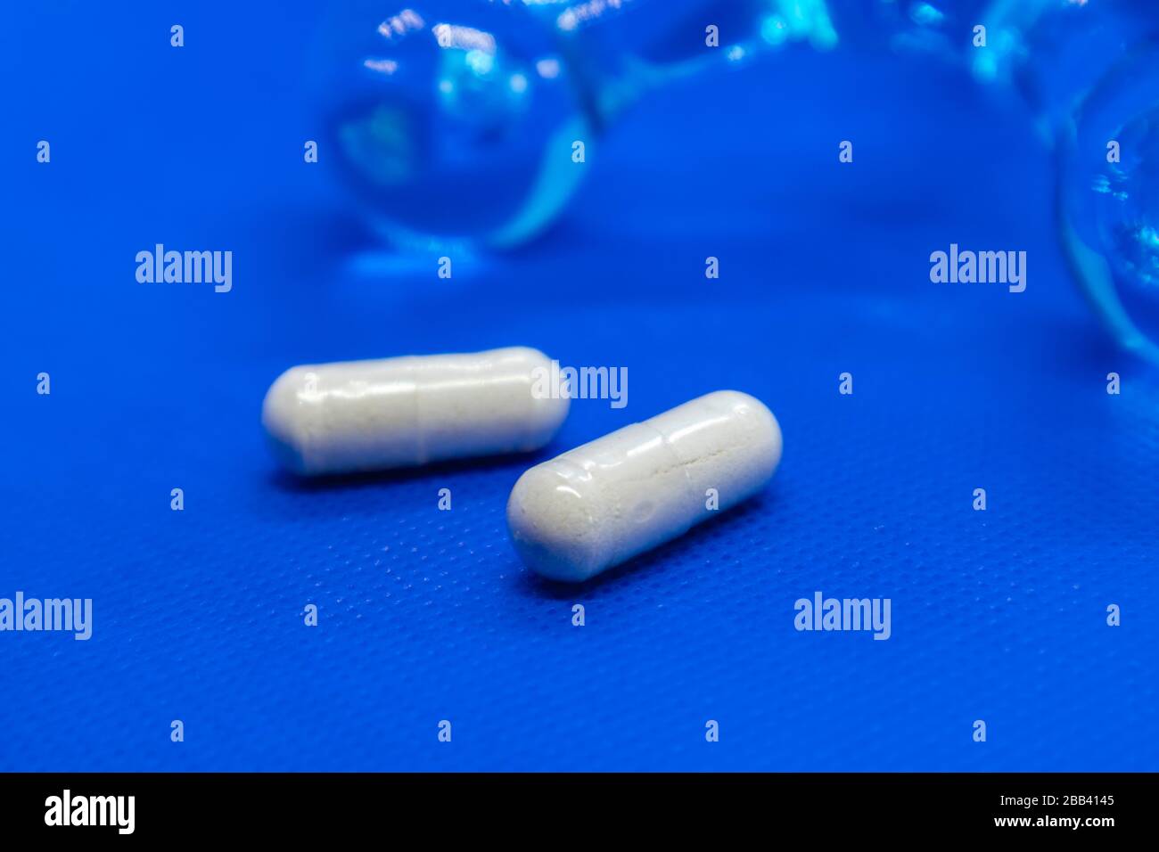 White long capsule pills supplement on blue background. Cure medicine ...