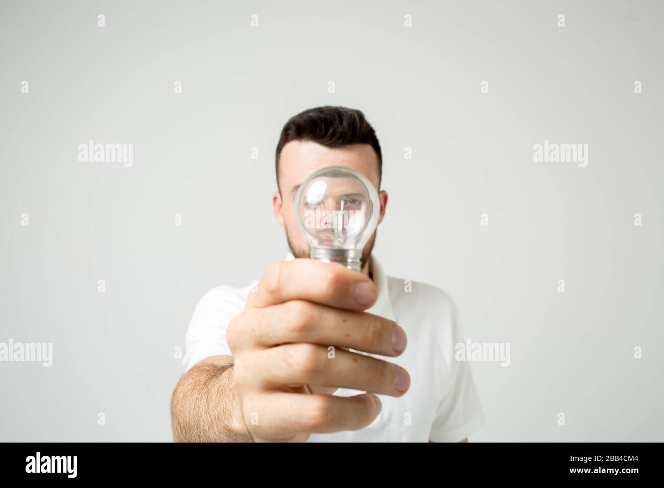 Young man in white shirt hold light bulb in hand and show it on camera ...