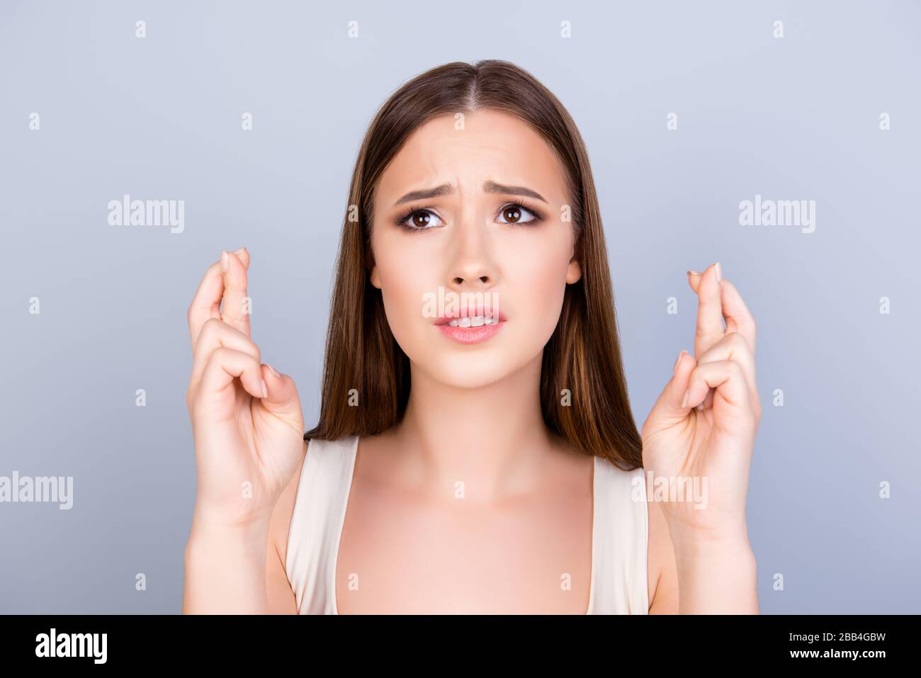 Young cute lady is keeping fingers crossed and looks up, hoping for ...