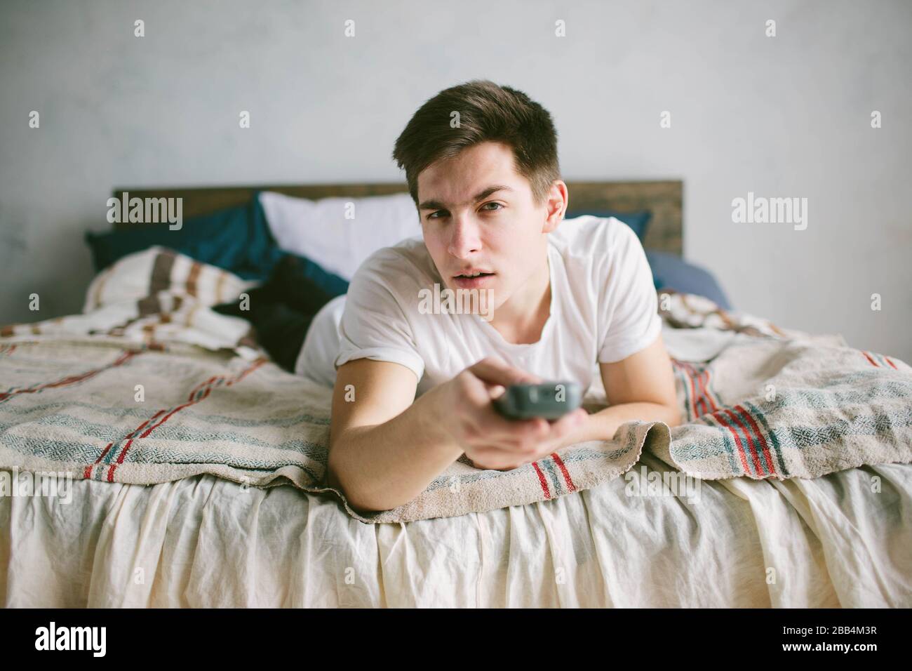 Guy using remote control while sitting on the bed in home. Happy ...