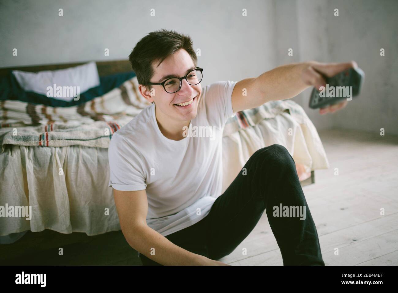 Guy using remote control while sitting on the bed in home. Happy ...