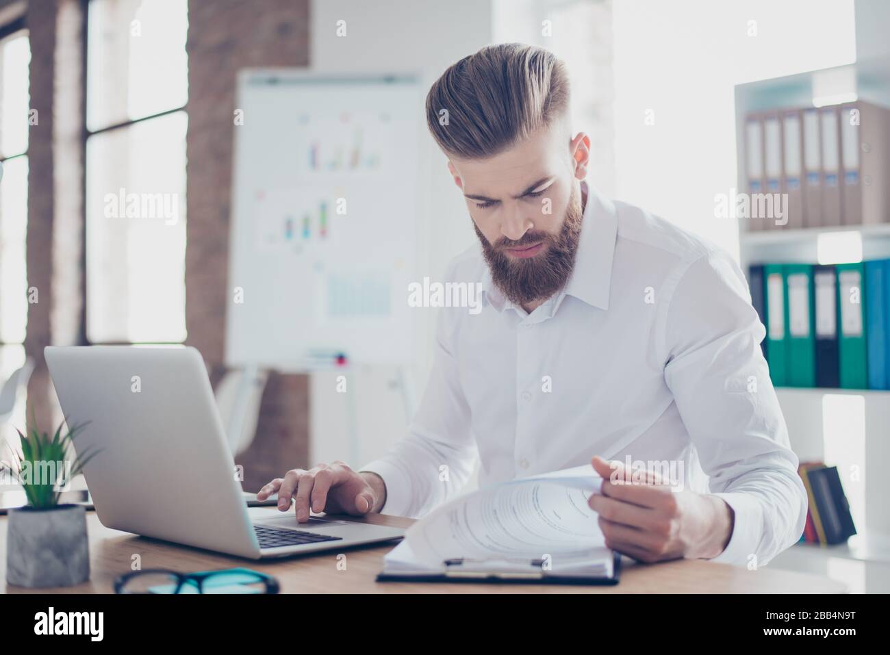 Concentrated young businessman is typing information from papers to his ...