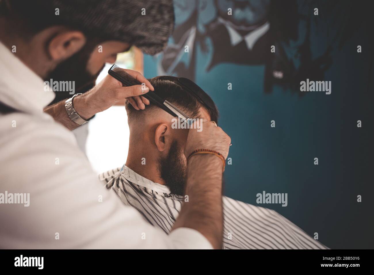 Stylish hairdresser in a cap does a haircut Stock Photo - Alamy