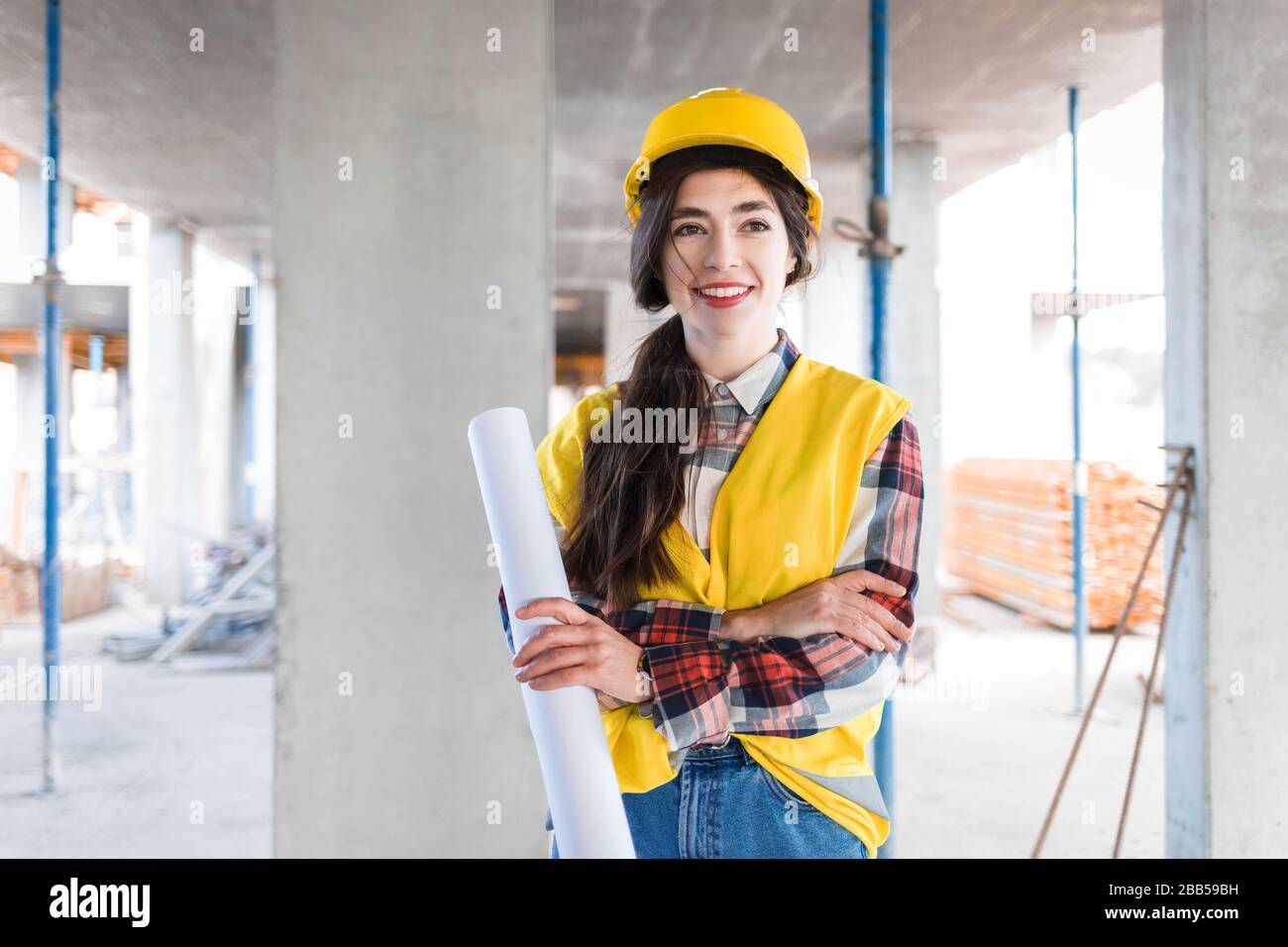 Confident girl engineer builder stands at a construction site holding ...