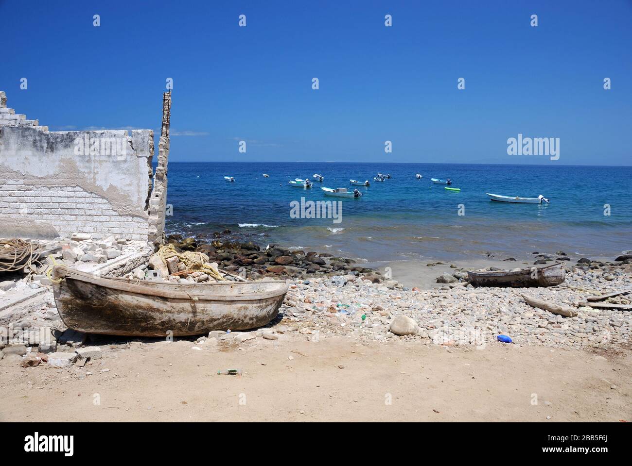 Old fisher wood canoe on dirty beach. Destroyed house on the left Stock ...