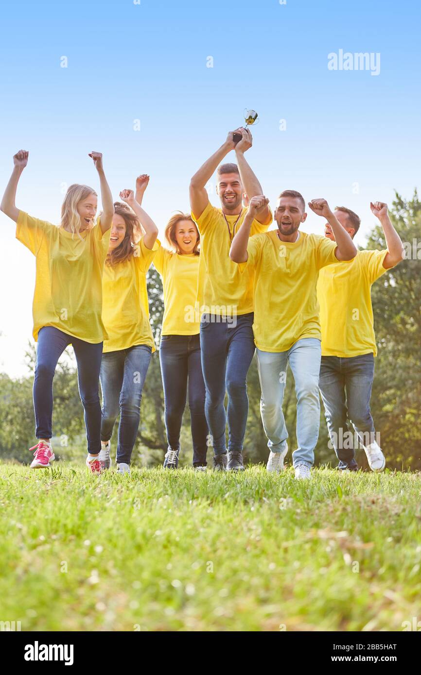 Happy winning team with cup cheers in a meadow at team building event ...