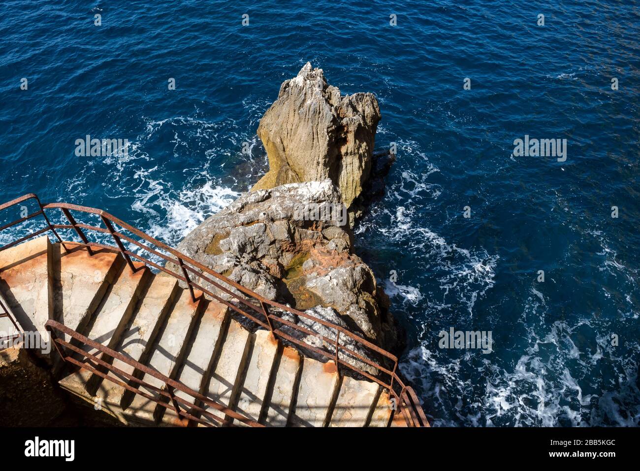 Old concrete stairs lining a cliff with a rusted handrail. Rock in the ...
