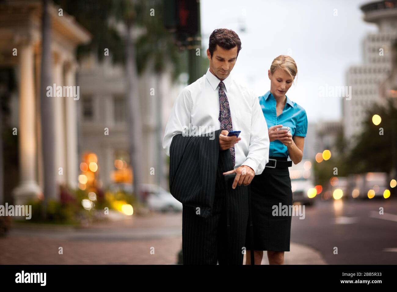 Two business colleagues looking at their cell phones while standing on ...